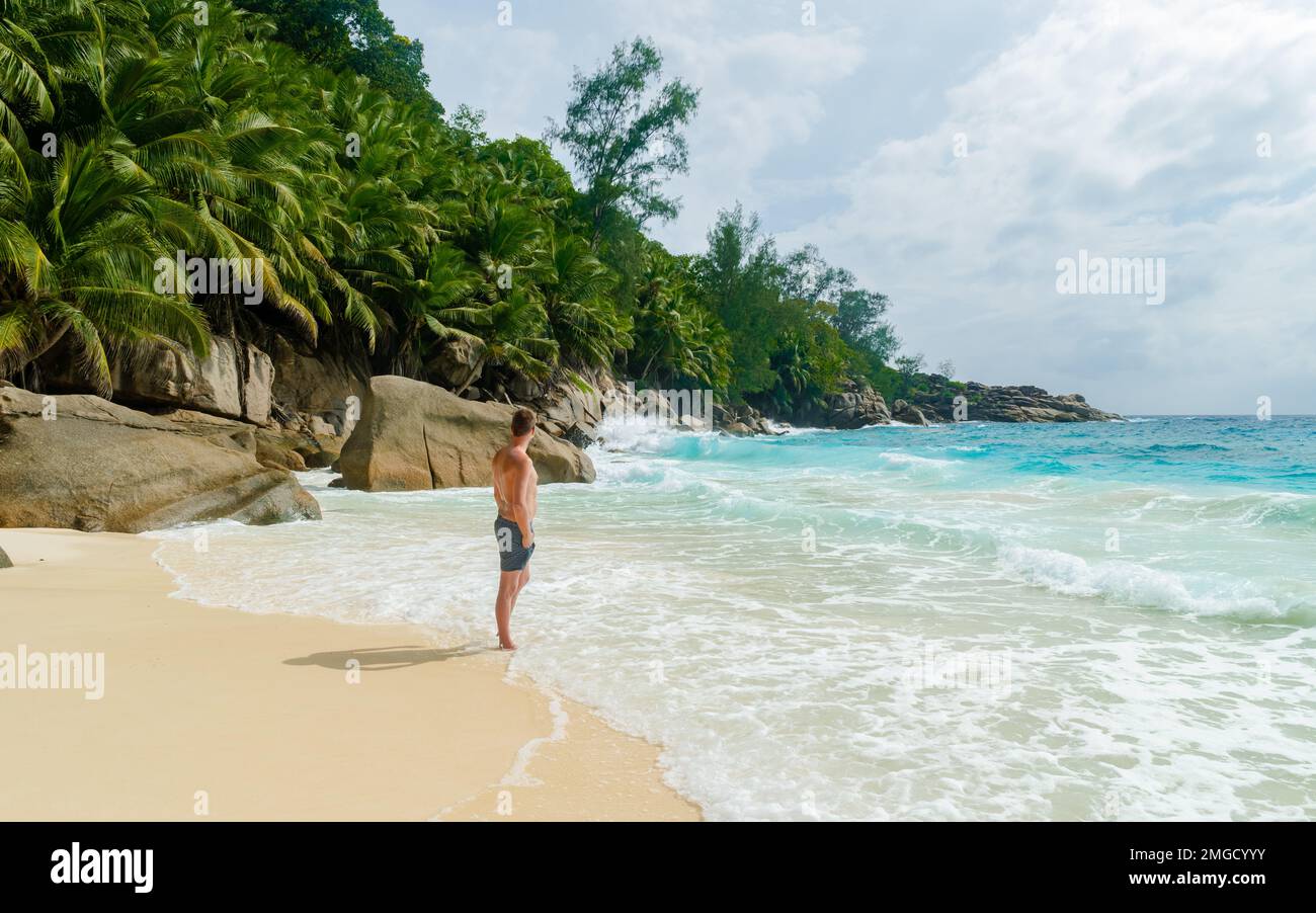 Young men in swim short on a white tropical beach with palm trees ...