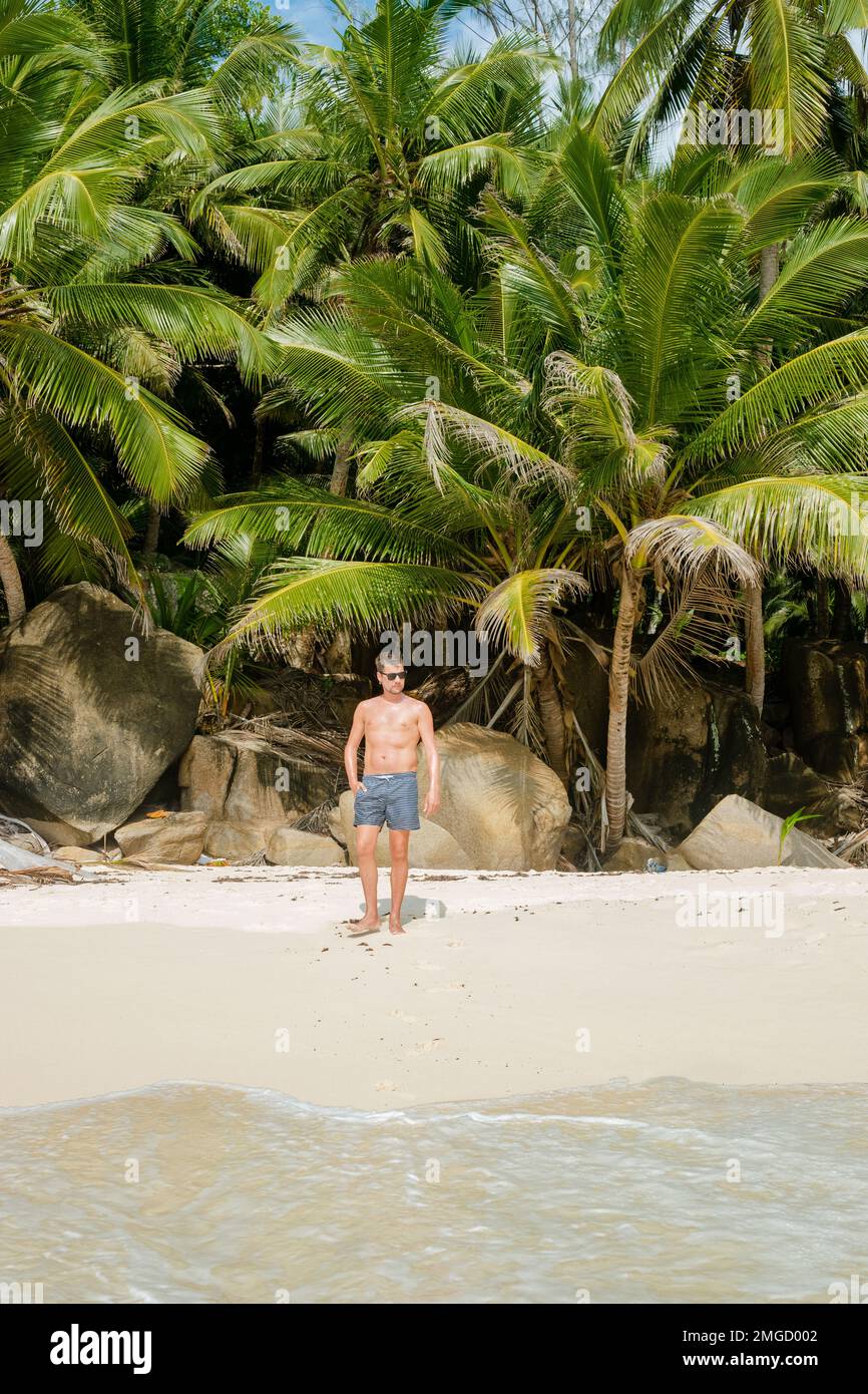 Young men in swim short on a white tropical beach with palm trees ...