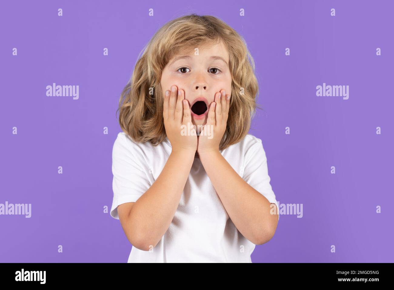 Shocked kid keeping hands near cheek with open mouth on studio isolated ...