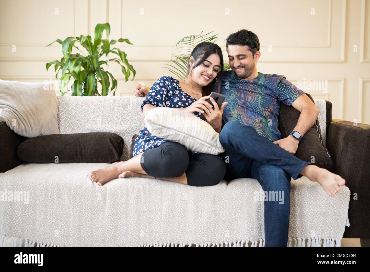 wide shot Portrait shot of happy smiling indian couple busy using mobile phone while sitting on ...
