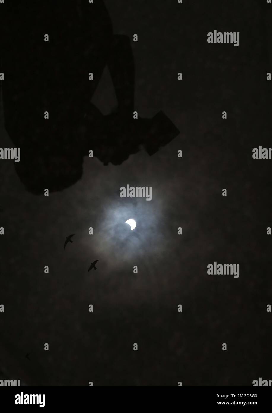 A photographer taking pictures of solar eclipse is reflected in rain ...