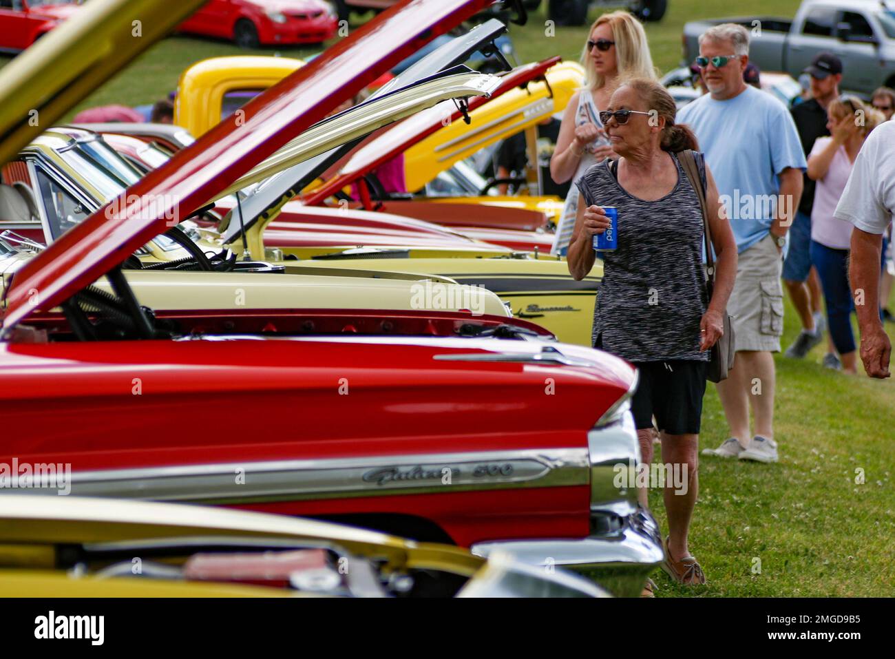 Visitors walk through a line of classic cars with their hoods up at a ...