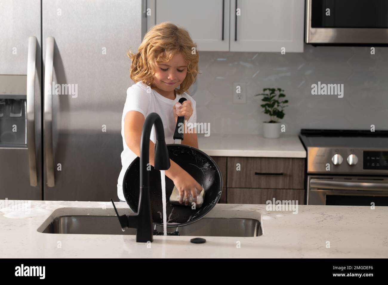 Home chores. Kid in kitchen cleaning plates. Cute boy washing dishes in ...