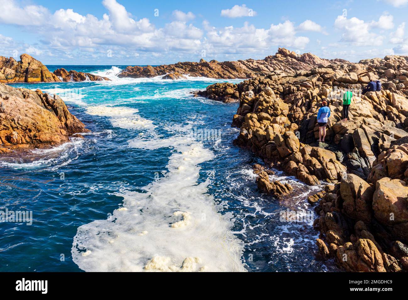 Tourists looking at the weathered channel of water through the granite ...