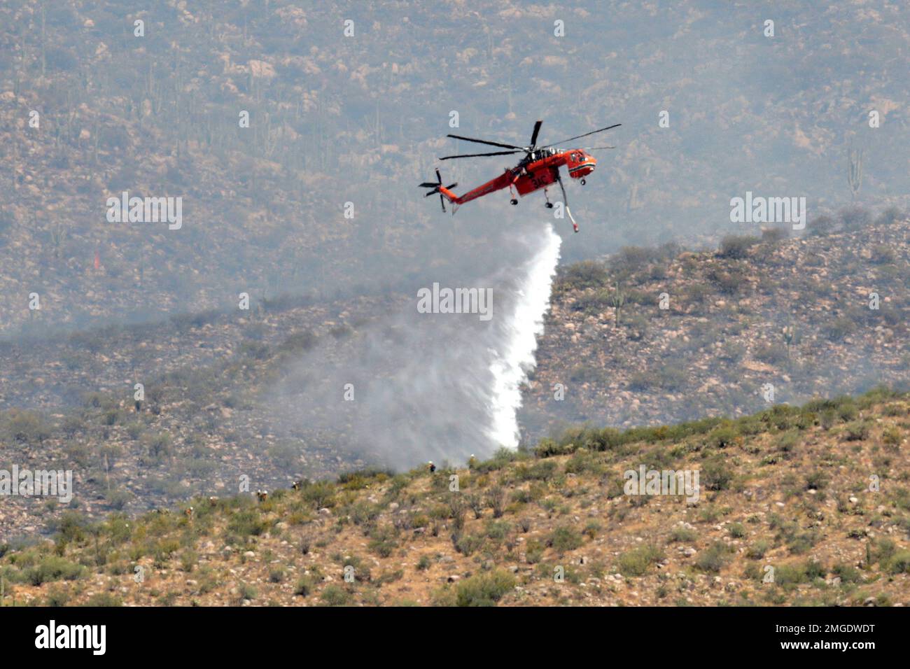 Heat ripples distort an air attack crew as they drop water on the ...