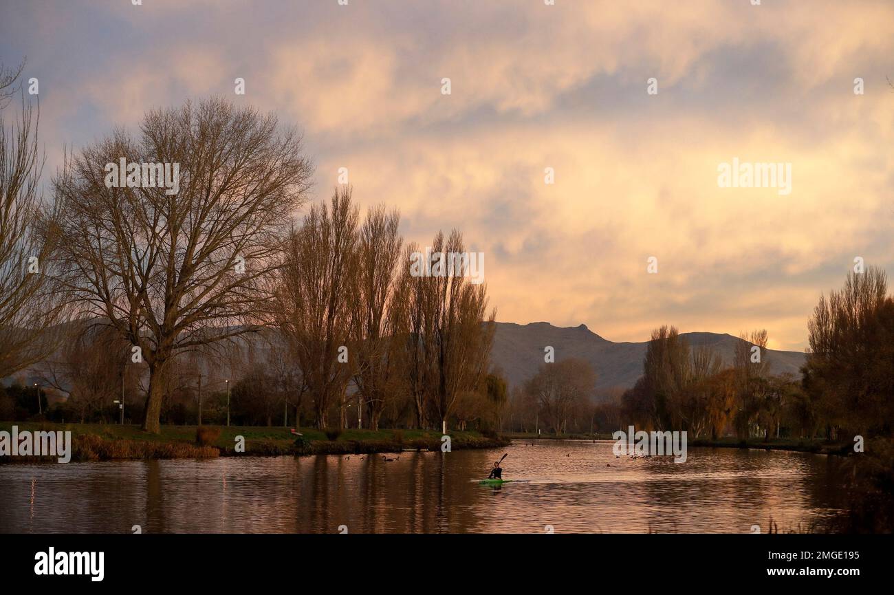 A woman paddles her kayak on the Avon River at sunset in Christchurch ...