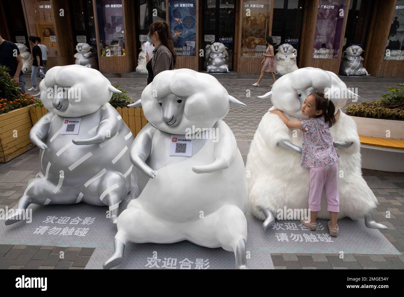 A child hugs a giant sheep sculpture along a popular retail street in ...