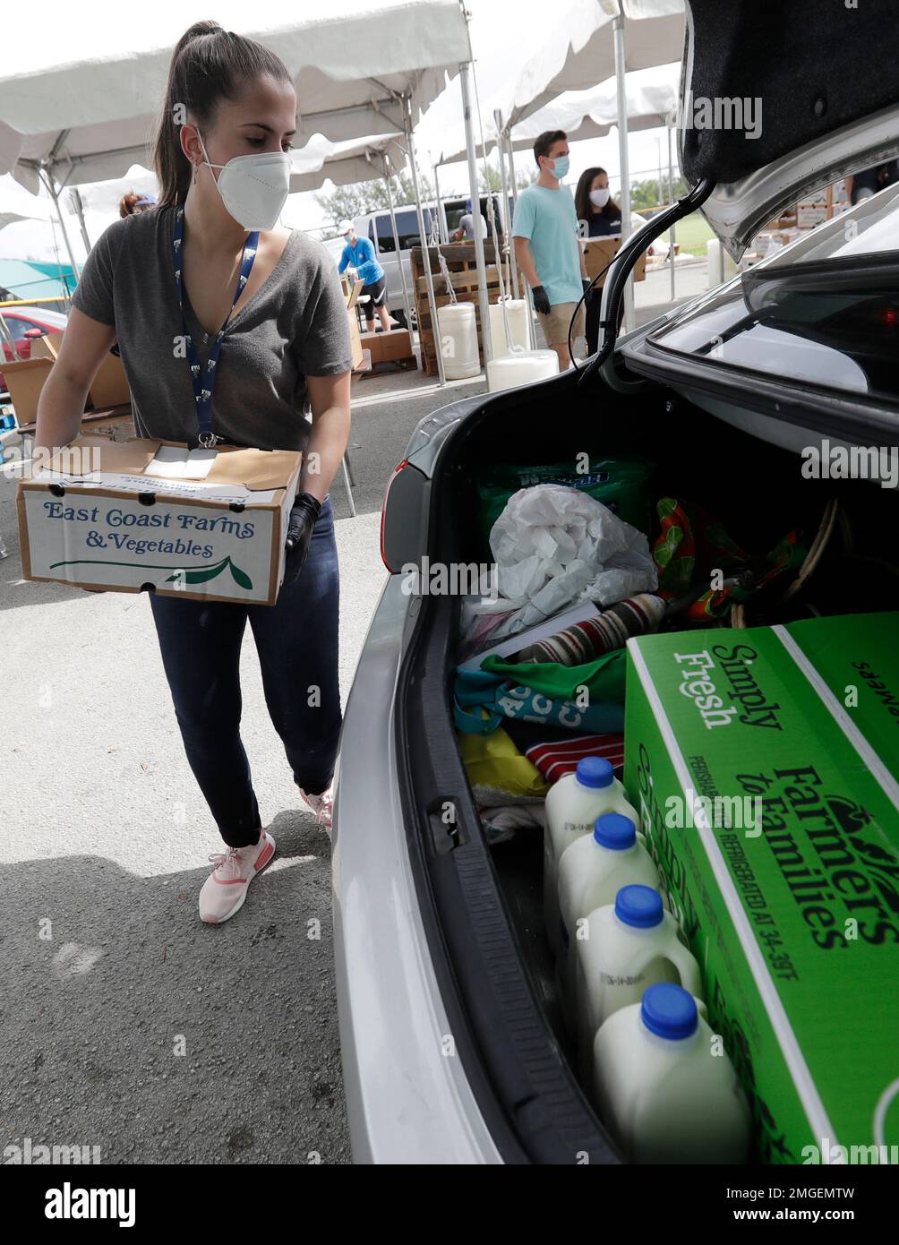A volunteers loads a box of food into a car lined up for a weekly food ...