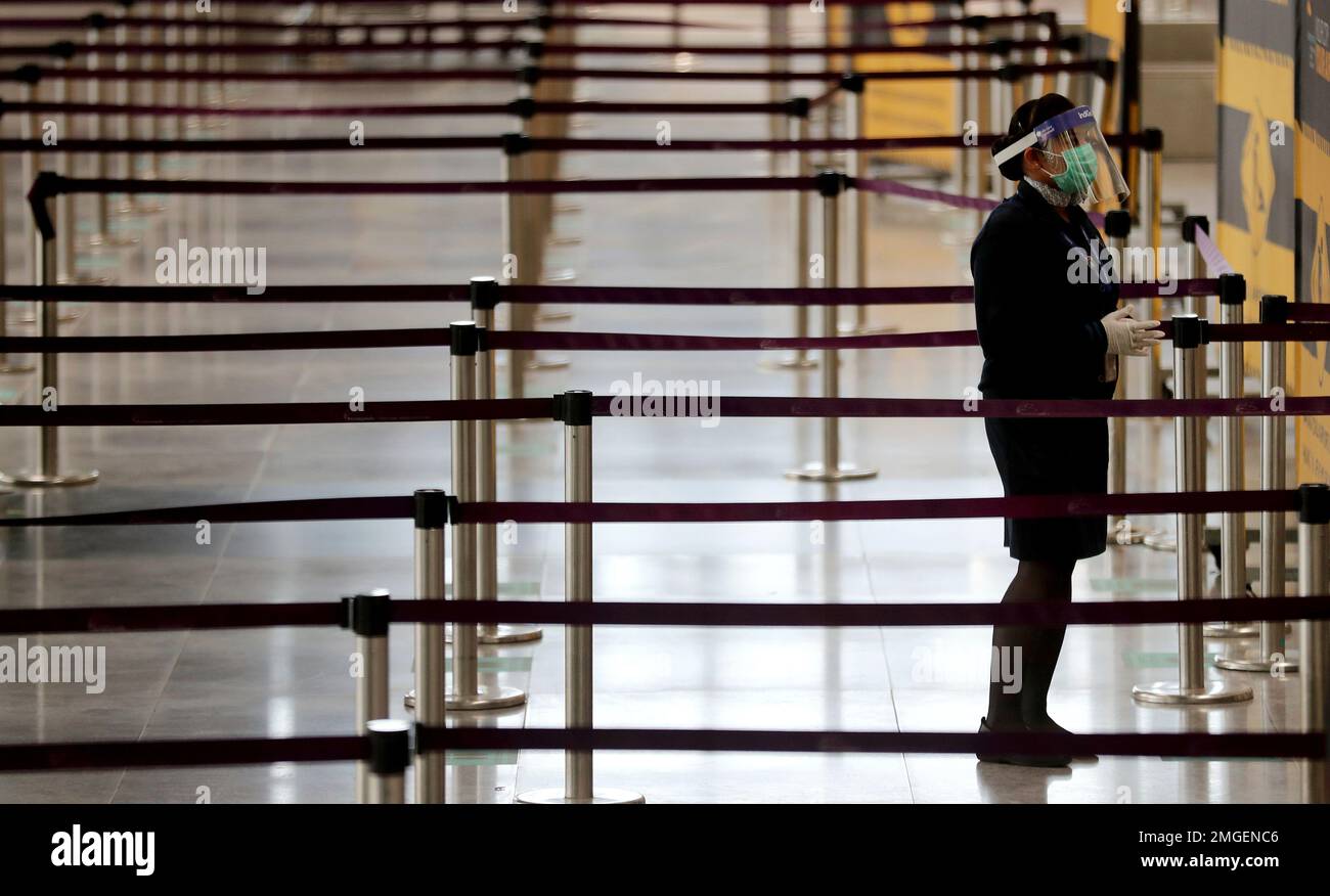 An airline staff member wearing face shield and mask waits between ...