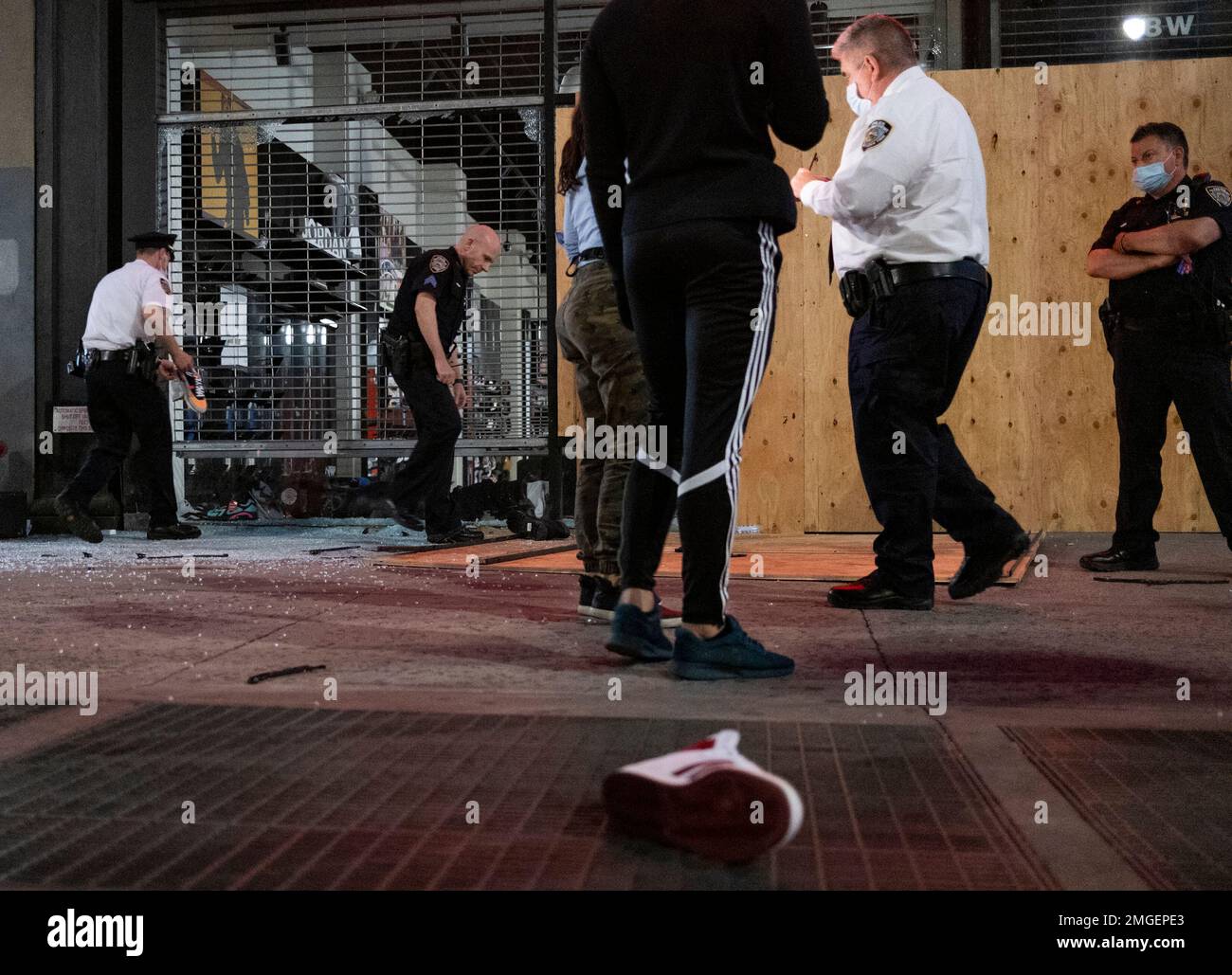 Police stand outside damaged stores after the glass was knocked out in ...
