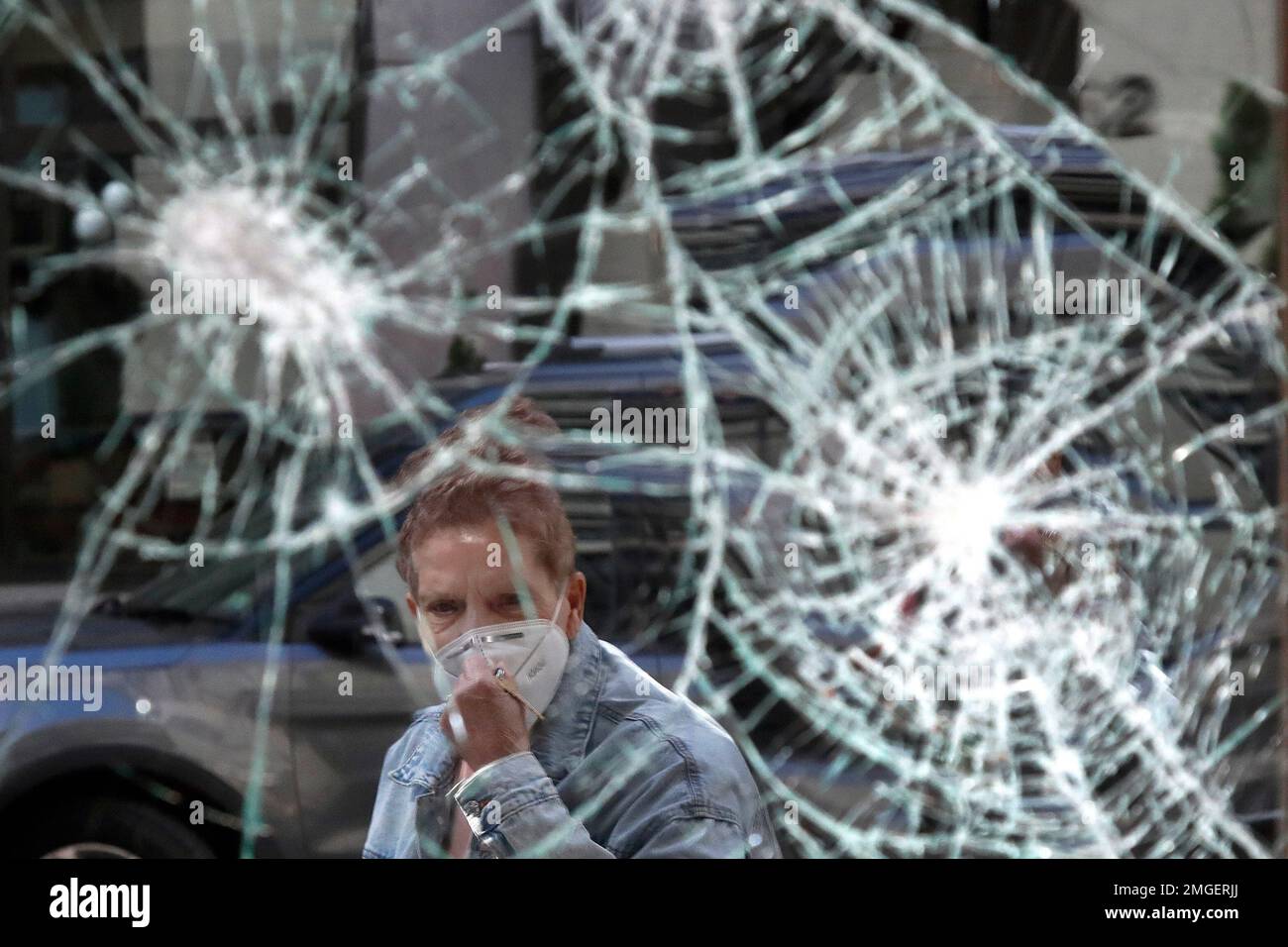 A woman wearing a mask due to coronavirus concerns, looks at a smashed ...