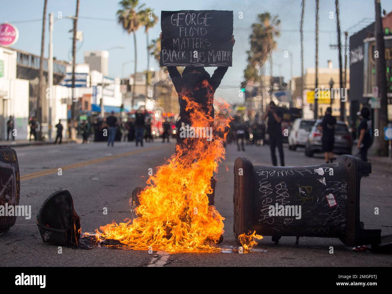 A protester holding a sign stands behind the burning trash cans during ...