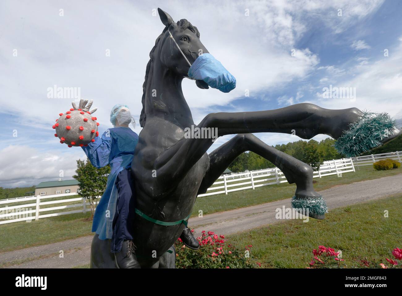 A statue of a horse with a mask, carries a rider in PPE holding a model ...