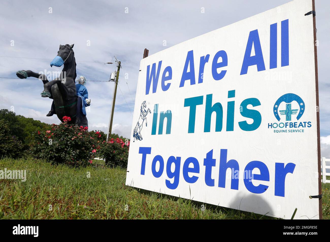 A statue of a horse with a mask, carries a rider in PPE holding a model ...