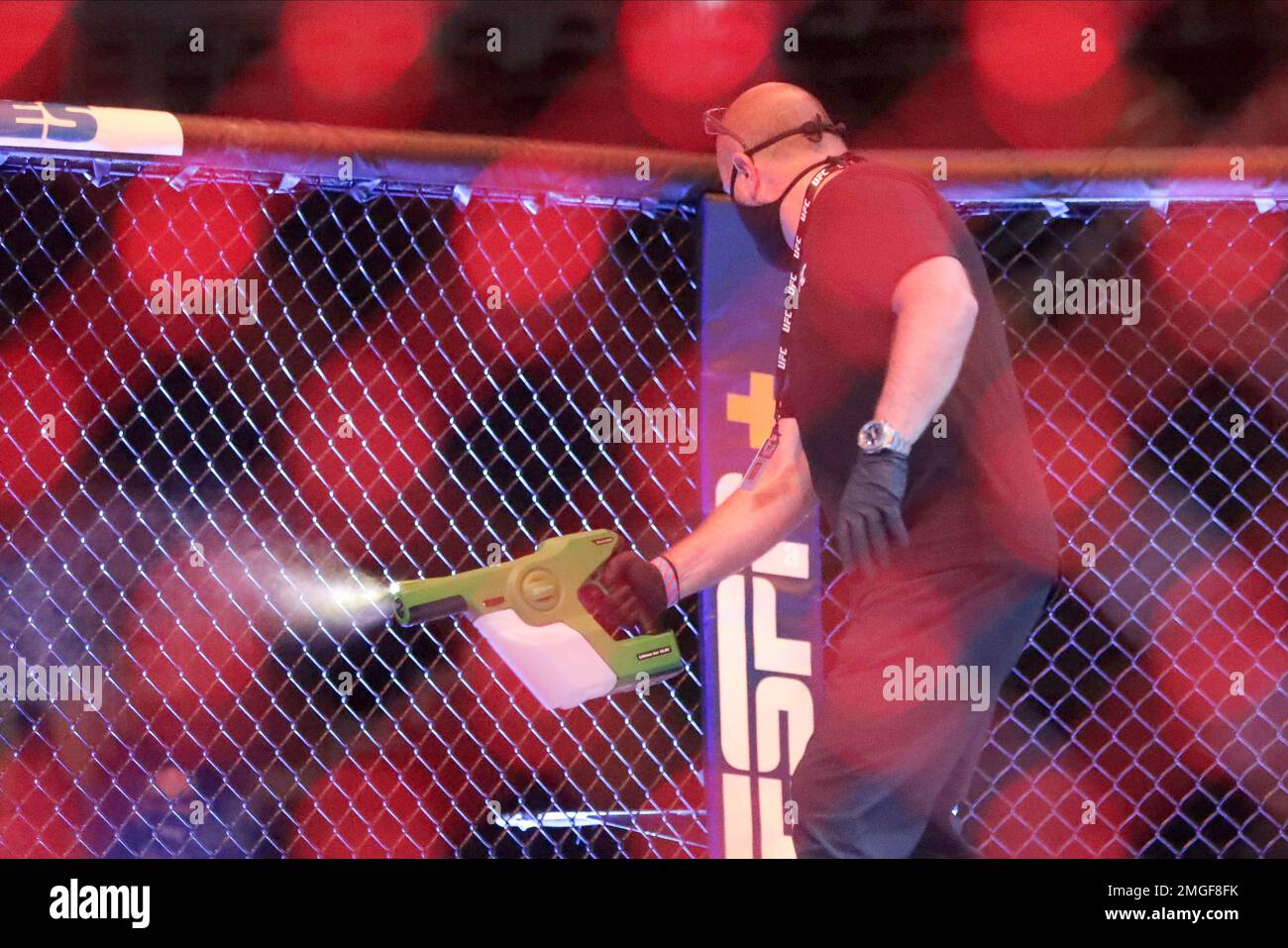 A worker sprays a sanitizer around the octagon between fights during a ...