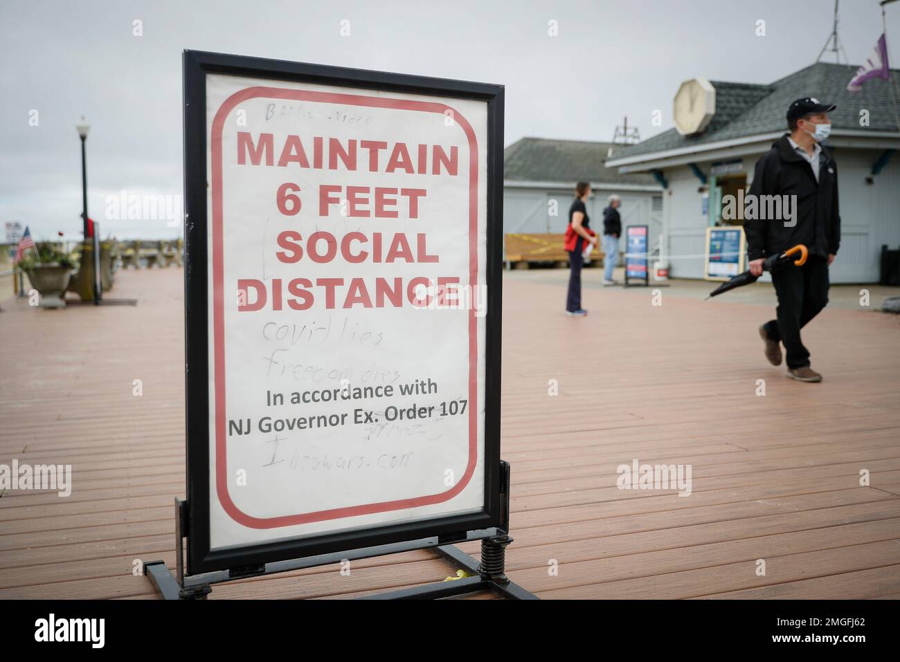 Pedestrians pass a social distancing sign along a mostly empty ...