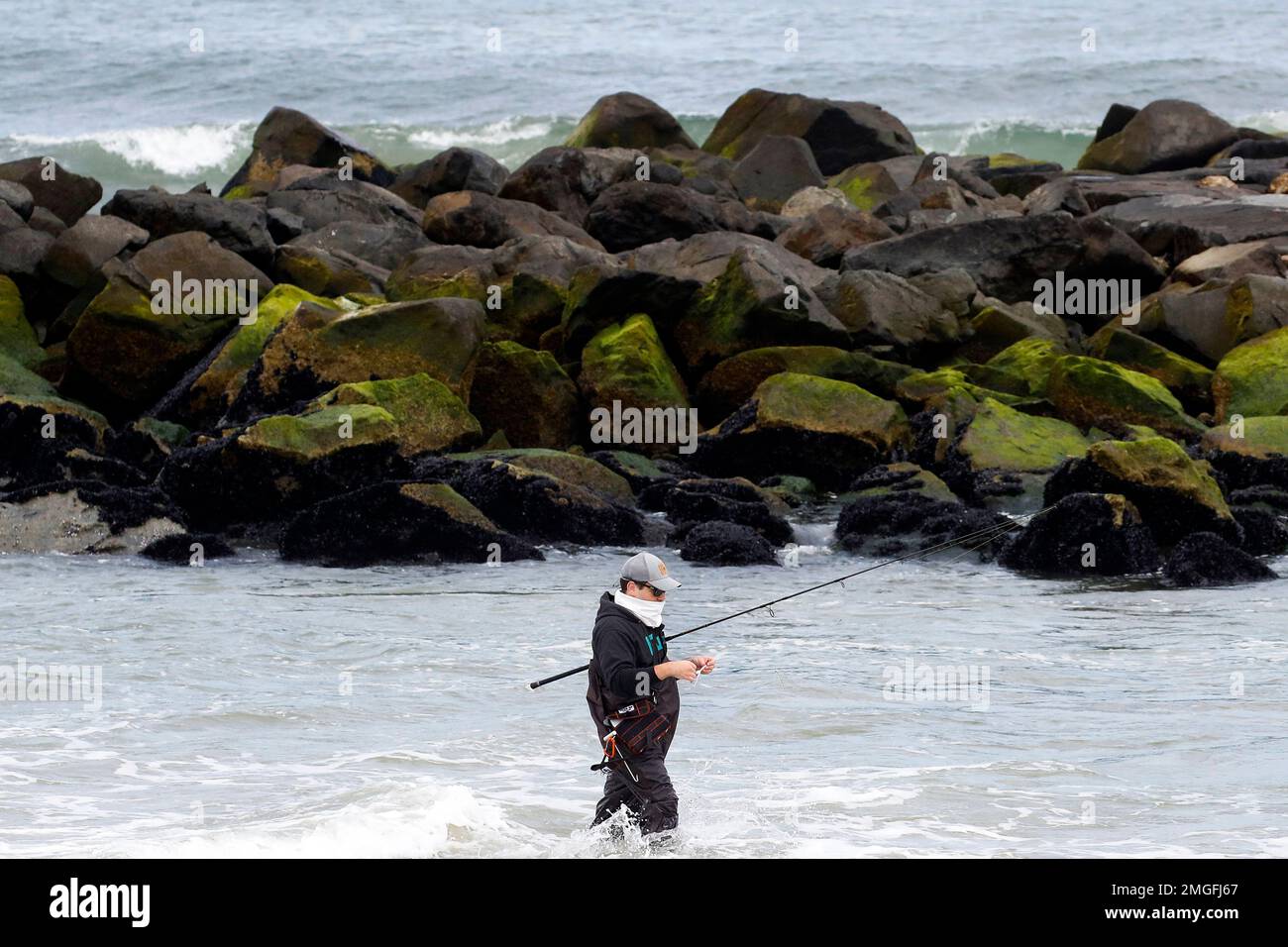 A fisherman wears mask as he resets his tackle at a mostly empty beach ...
