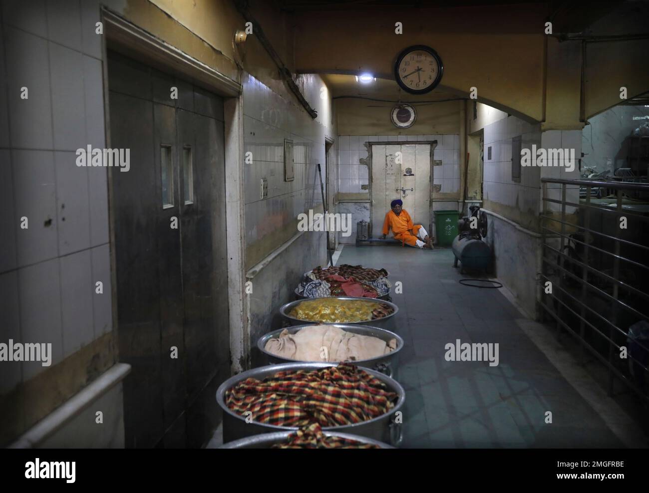 A Sikh cook rests as large vessels containing cooked rice lie covered ...