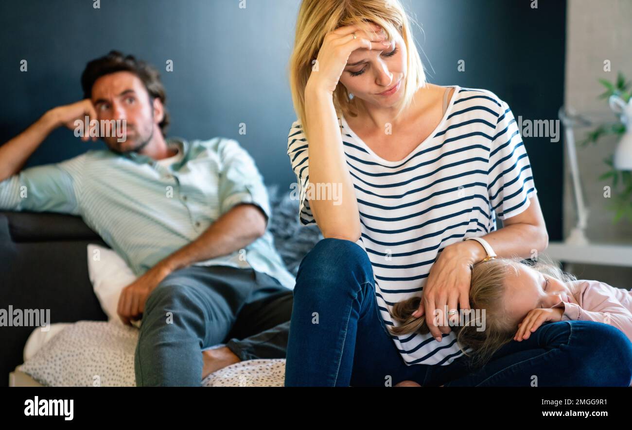 Tired mother and father sitting on couch feels annoyed exhausted stressful with little girl ...