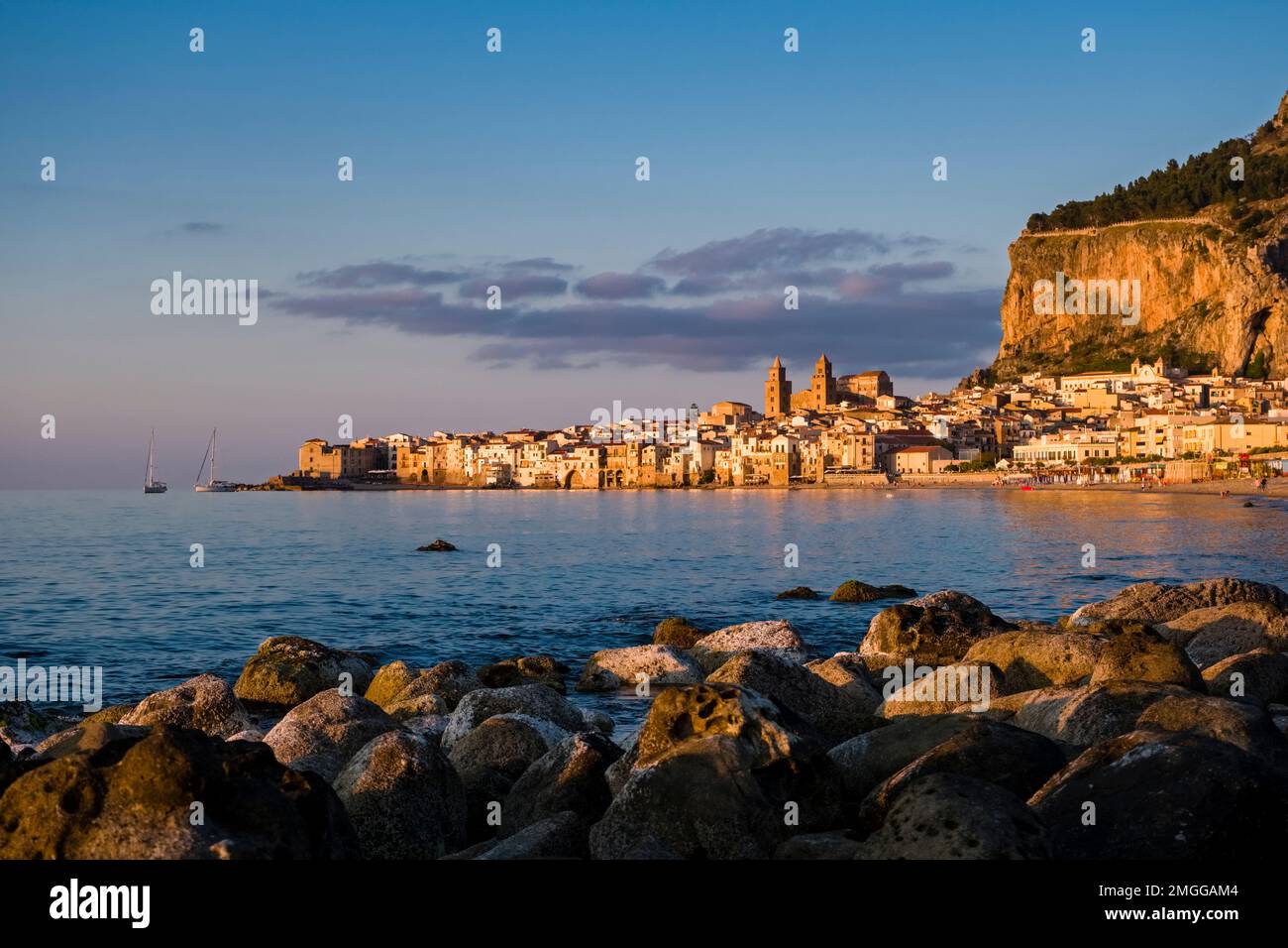 View across some rocks and the sea to the medieval town of Cefalu ...