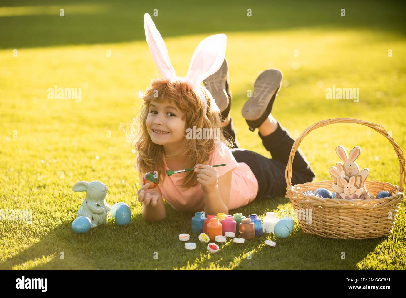 Easter kid in park. Child boy with easter eggs and bunny ears laying on ...