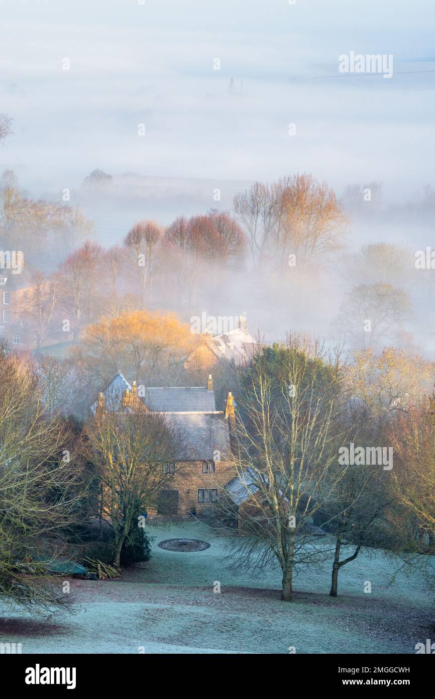 Winter morning sunlight over a foggy frosty Arlescote village in the ...