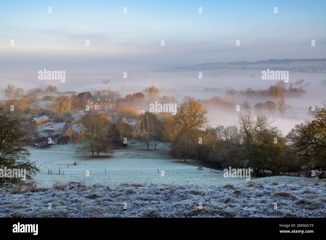 Winter morning sunlight over a foggy frosty Arlescote village in the ...