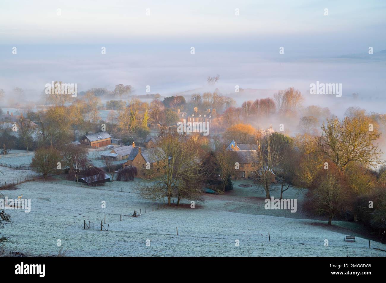 Winter morning sunlight over a foggy frosty Arlescote village in the ...