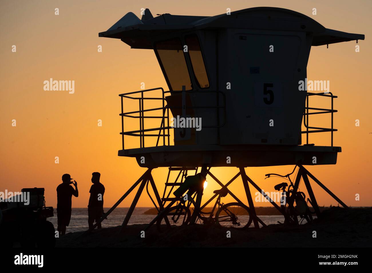 A man adjusts his mask as he and another man watch the sunset Monday ...