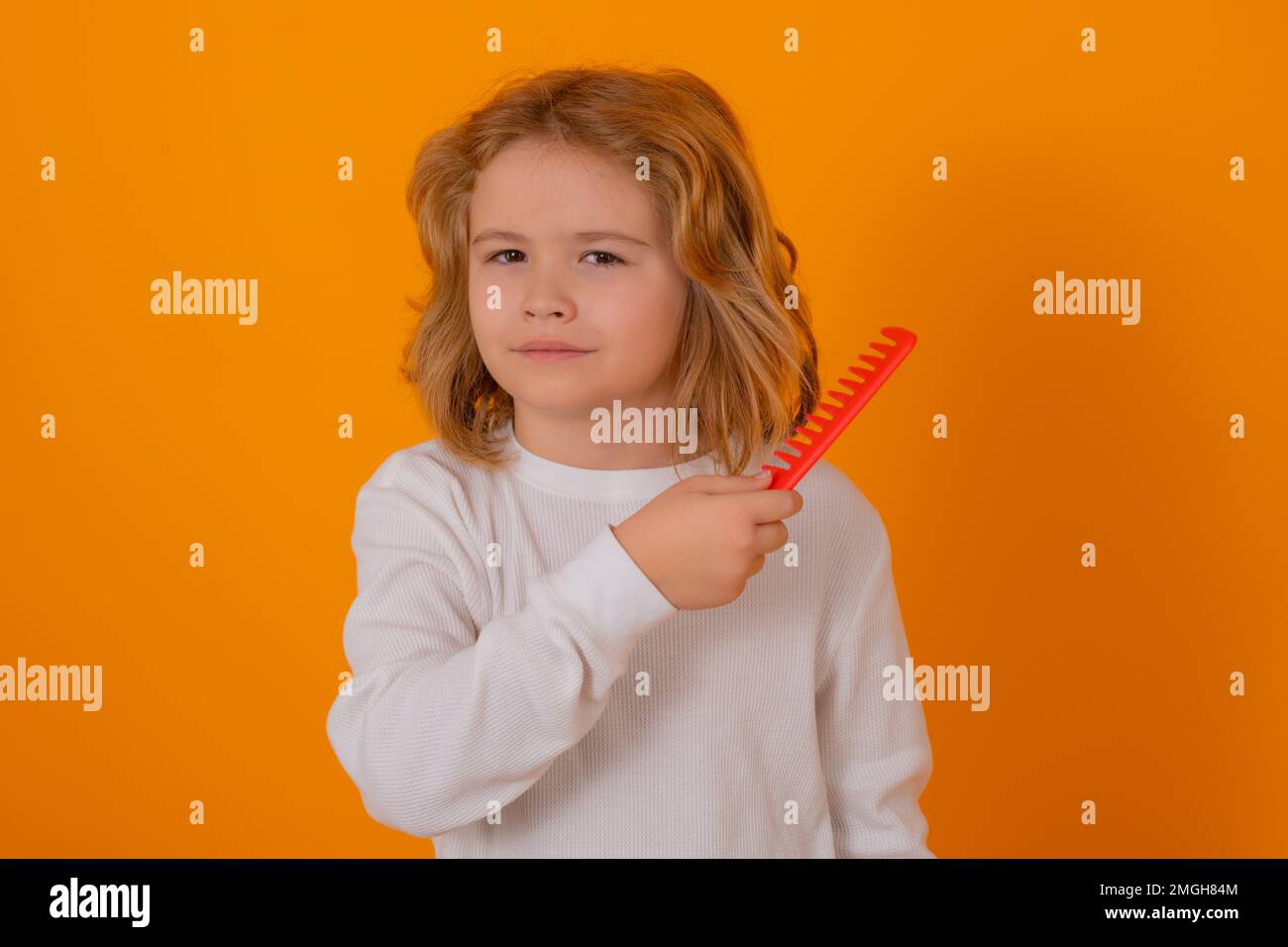 Portrait of child combing hair with comb on yellow studio background ...
