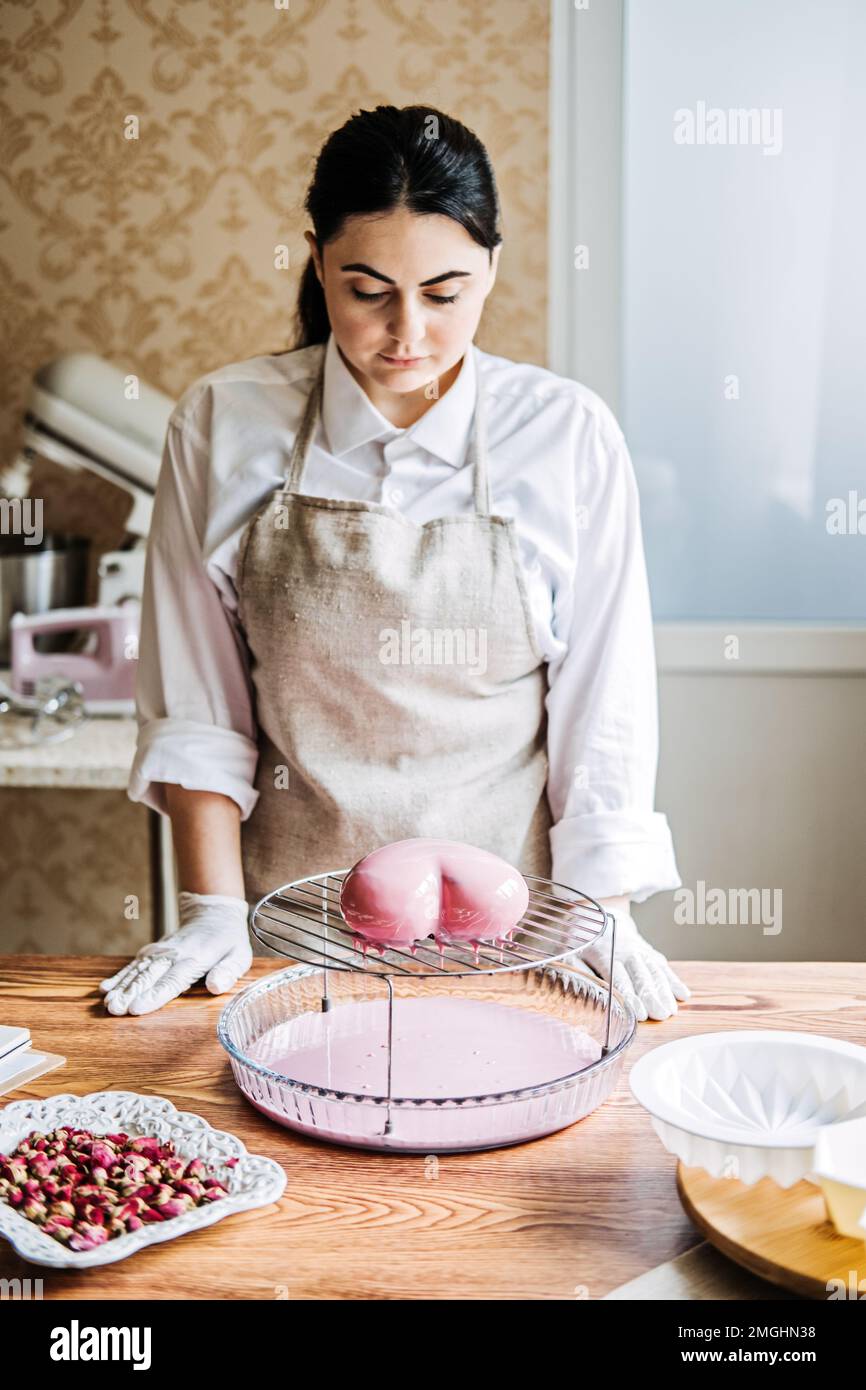 Female baker make Perfect custom pink heart shape cake in kitchen Bakery. Online Cake Store ...