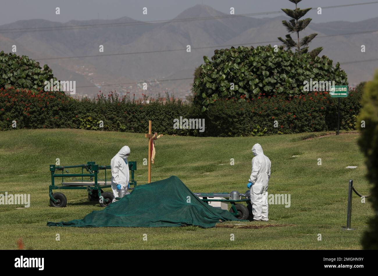 Cemetery workers wearing protective gear stand next to a coffin during ...