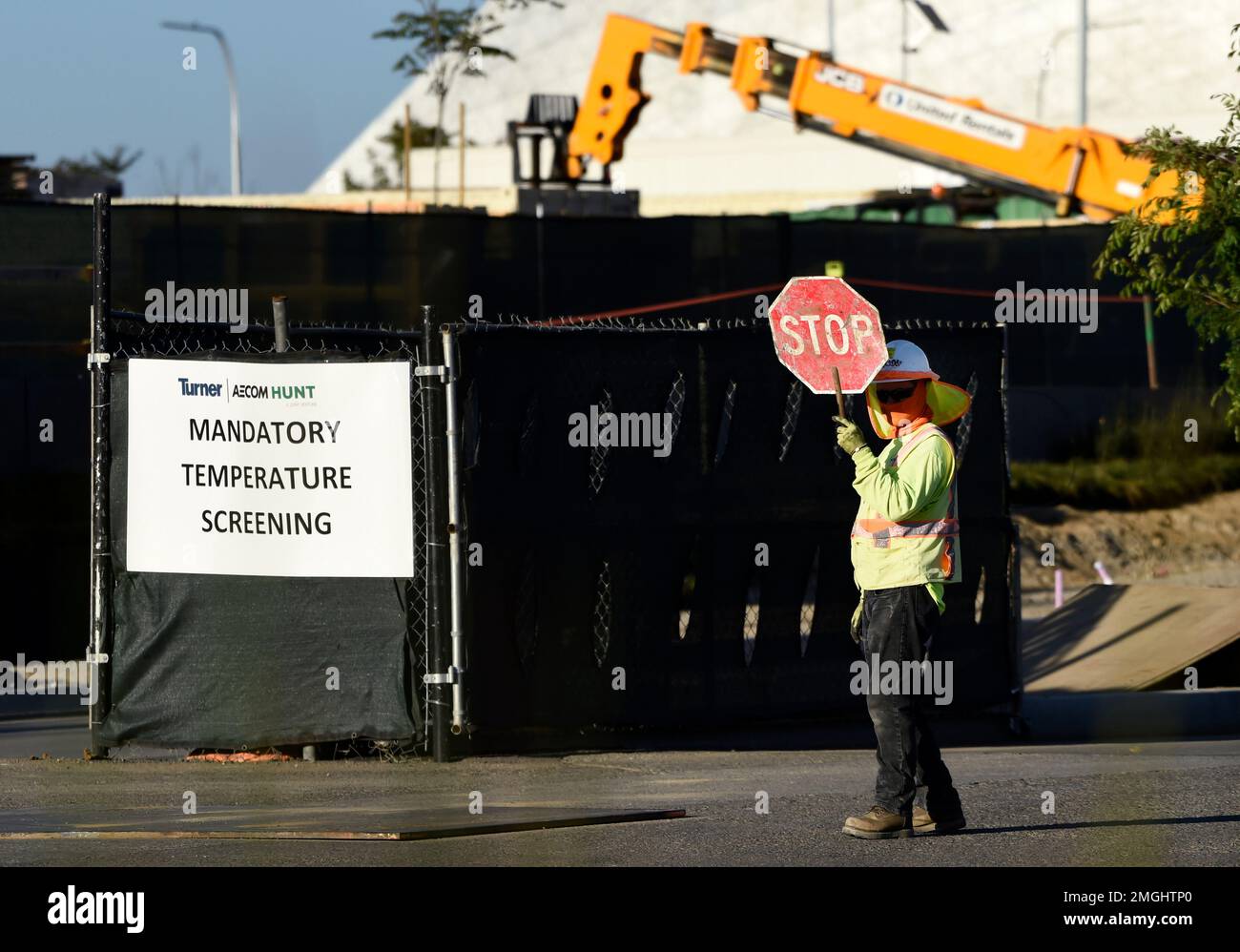 A worker directs traffic near a sign calling for mandatory temperature ...