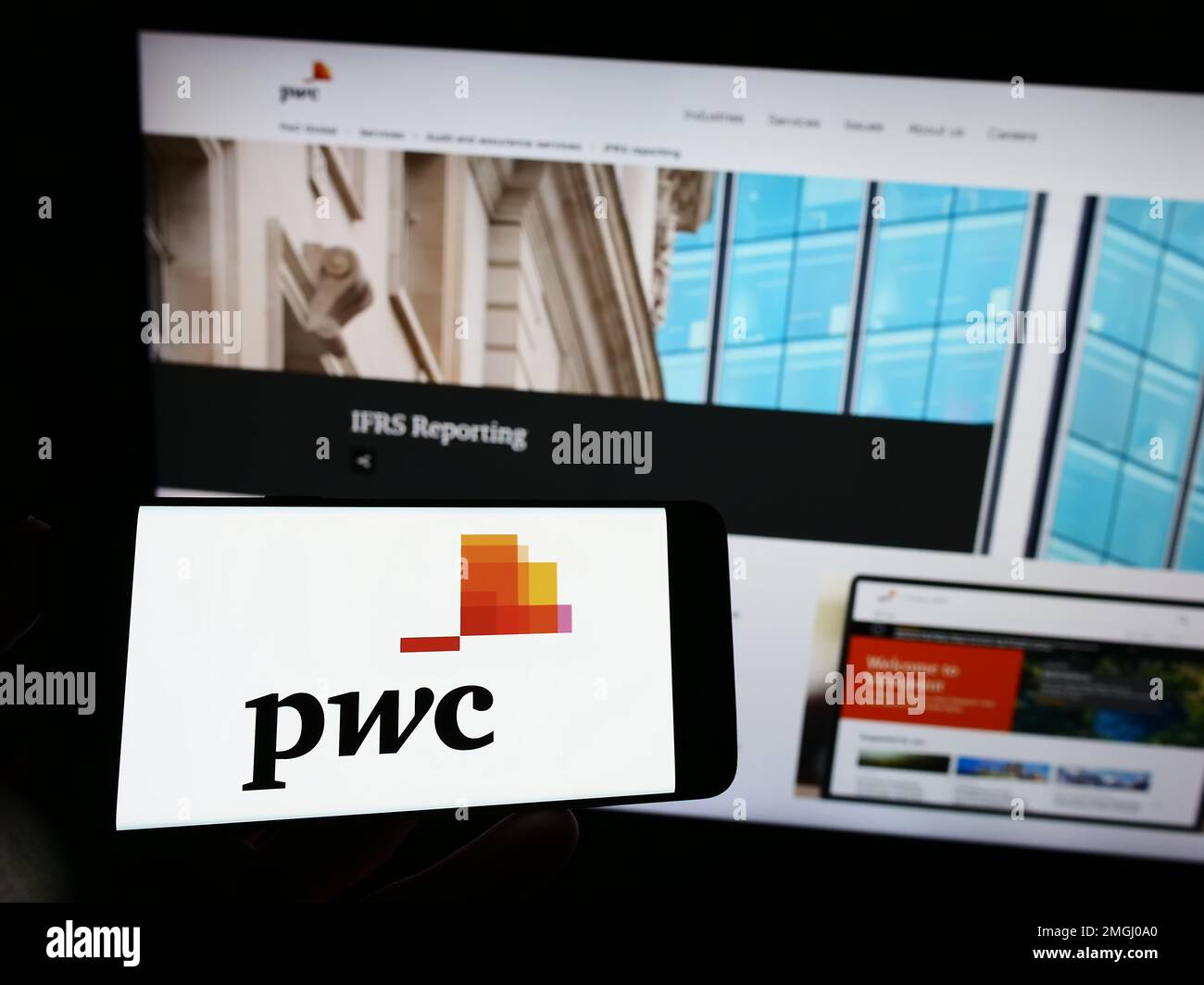 Person holding mobile phone with logo of consulting company PricewaterhouseCoopers (PWC) on ...