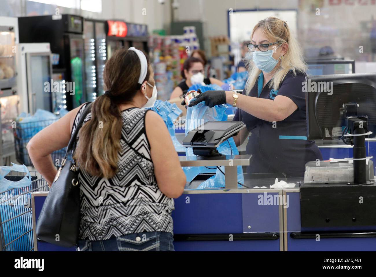 Cashier Mercedes Peña wears a protective mask as she works behind a ...