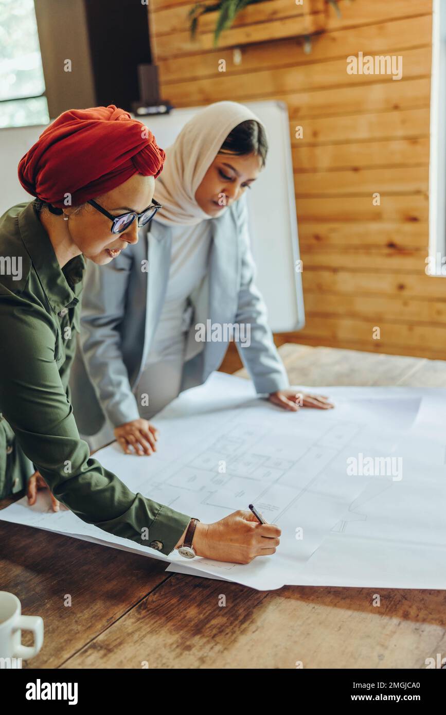 Two Muslim designers working on blueprint drawings in a modern office. Innovative businesswomen ...
