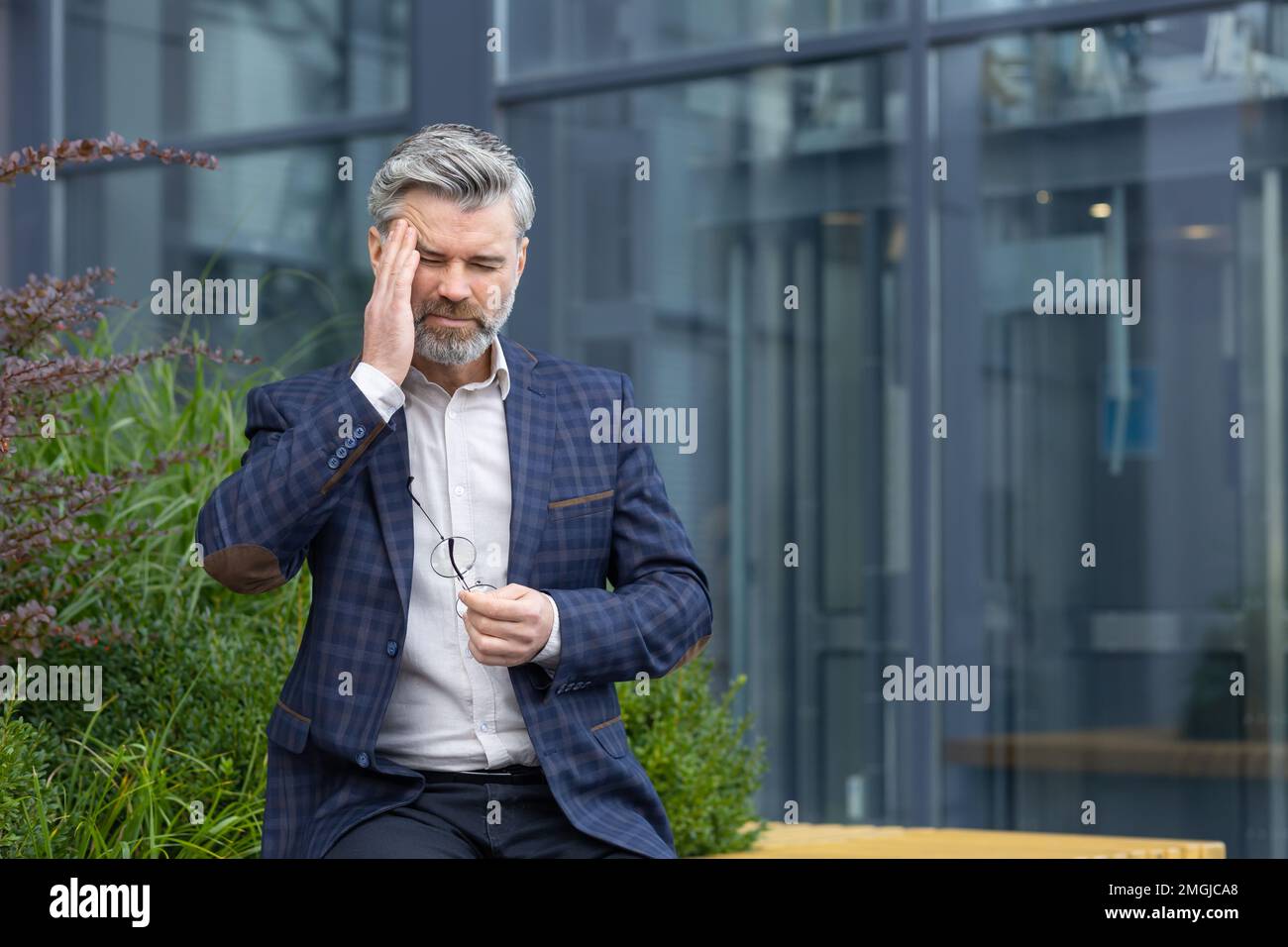 Sick and sad mature businessman outdoors sitting on bench on office ...