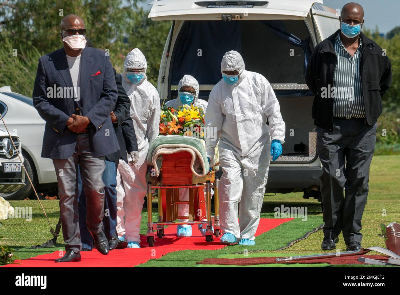 Pallbearers wearing full PPE suits lift the casket containing the ...