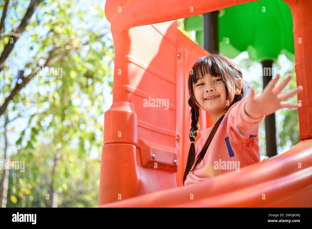 Joyful and happy little Asian girl is on slide, playing on playground ...