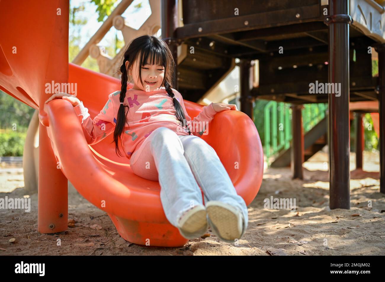 Cute and joyful Asian girl playing on playground, sliding on slider ...