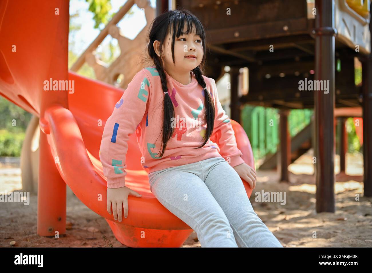 Cute and adorable Asian girl playing on playground, sliding on slider ...