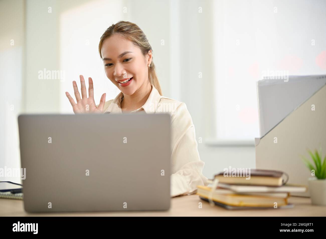 Happy and friendly millennial Asian businesswoman waves her hand to say ...