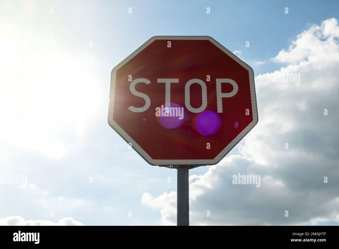 Red stop sign on metal pole on street. Road attention sign on cloudy ...