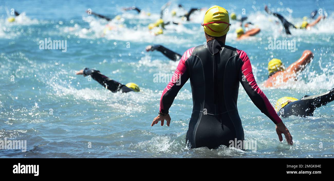 Group triathlon participants running into the water for swim portion of ...