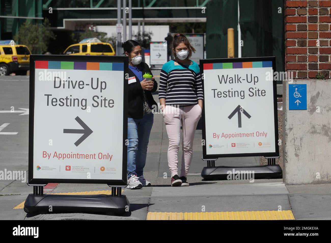 Women wear masks while walking between signs advising COVID-19 drive up ...
