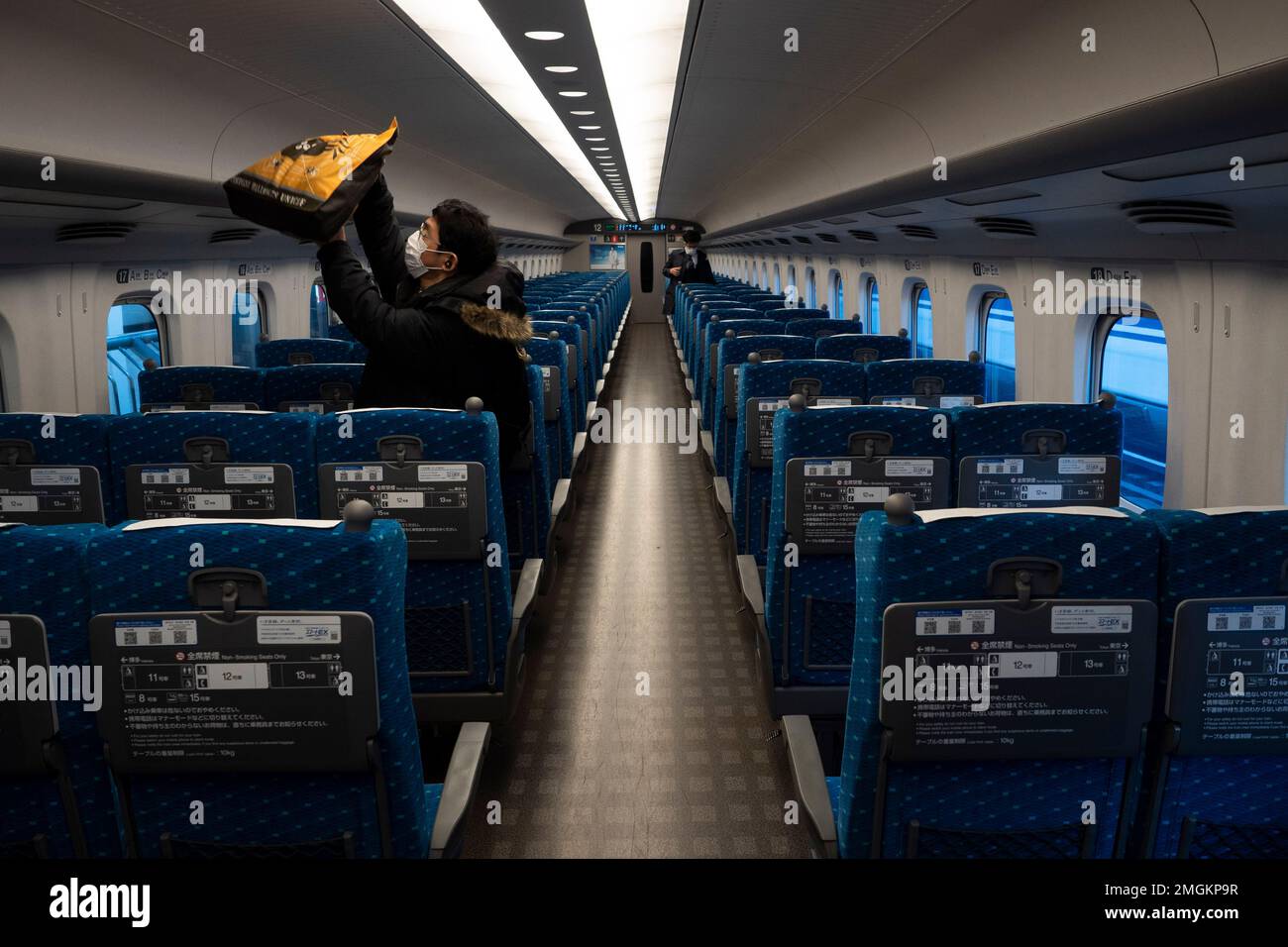 A traveler places his bag in an overhead luggage rack in a bullet train ...