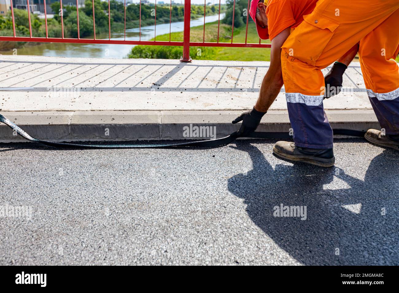 Workers attach a bitumen black tape to protect the roadside of bridge ...