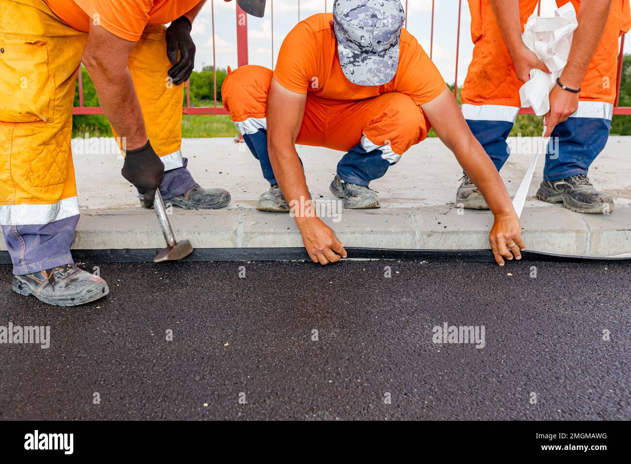 Workers attach a bitumen black tape to protect the roadside of bridge ...