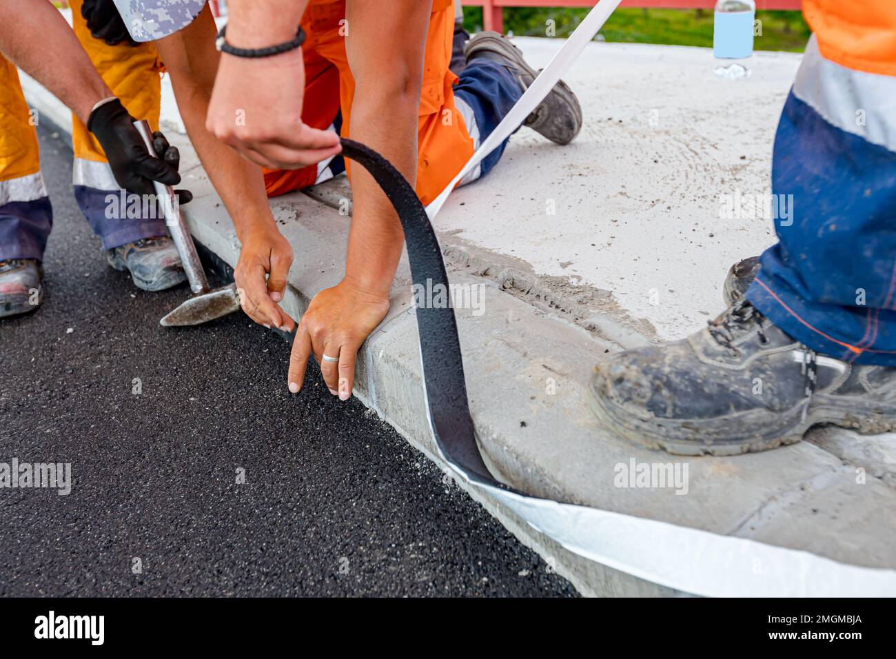 Workers attach a bitumen black tape to protect the roadside of bridge ...