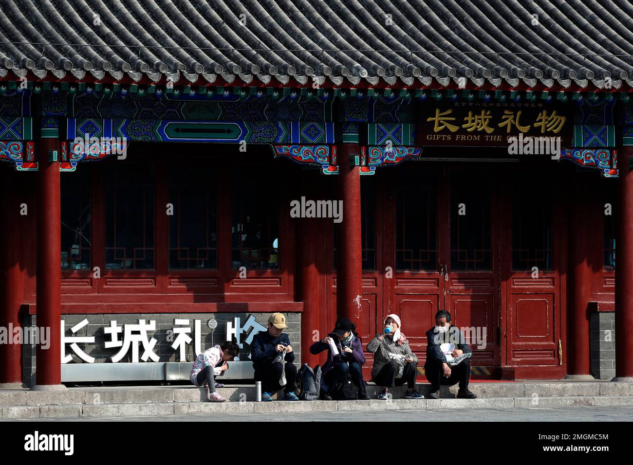 Visitors wearing protective face masks take a rest outside a shuttered ...